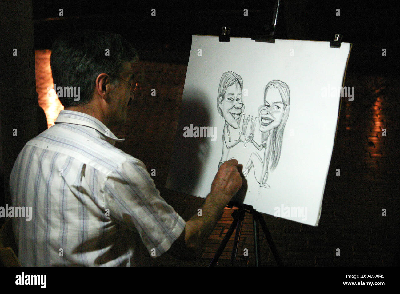 Street artist drawing picture of two young children at night lit by ...