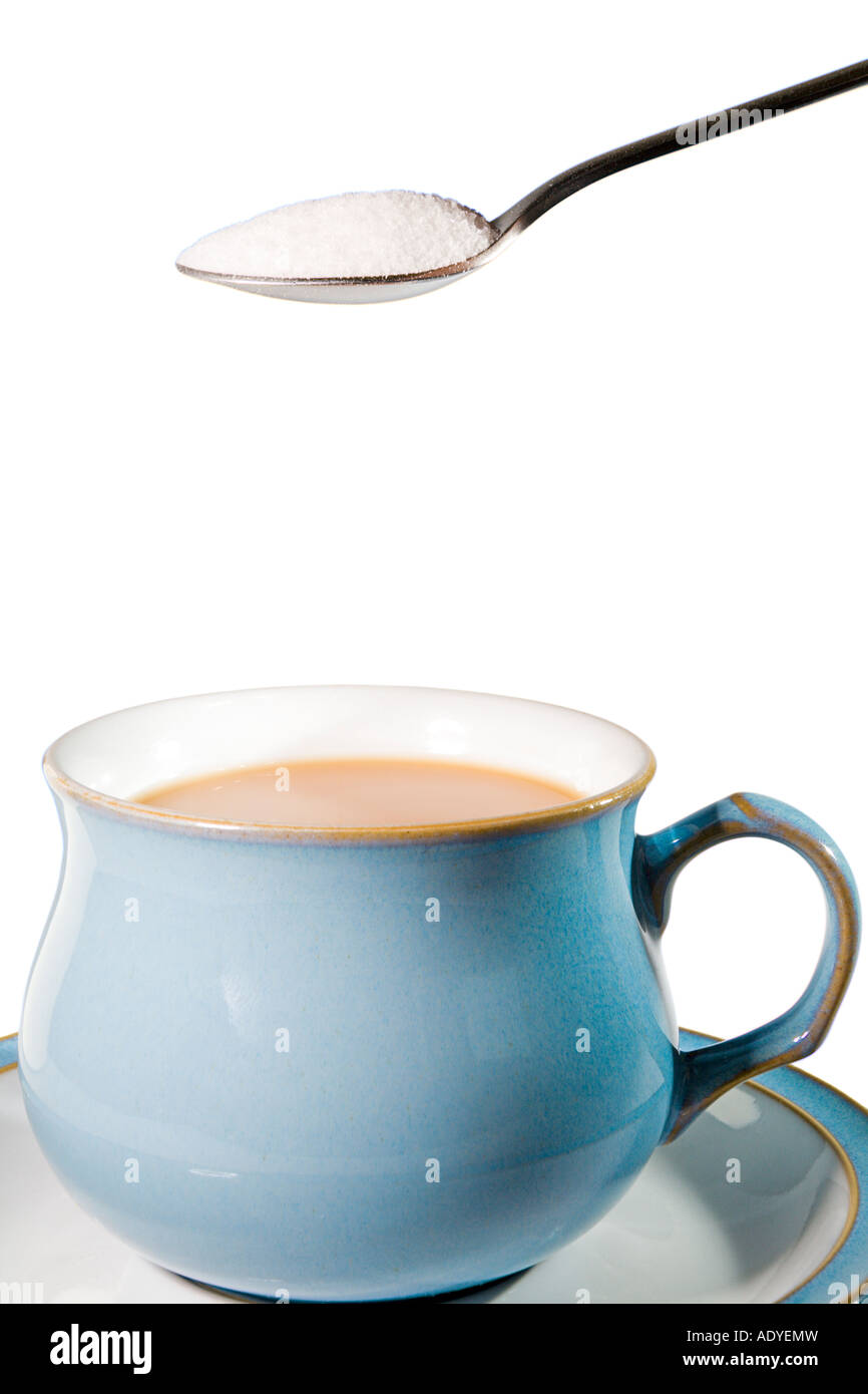 Pouring sugar from silver spoon into cup of hot English tea on saucer ...