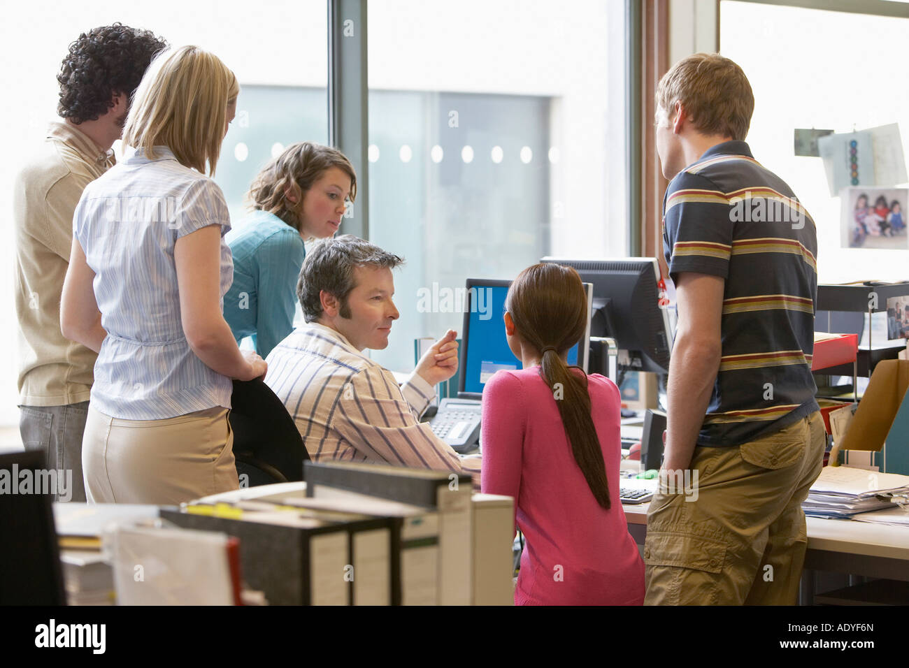 Office workers standing around colleague using computer, back view ...