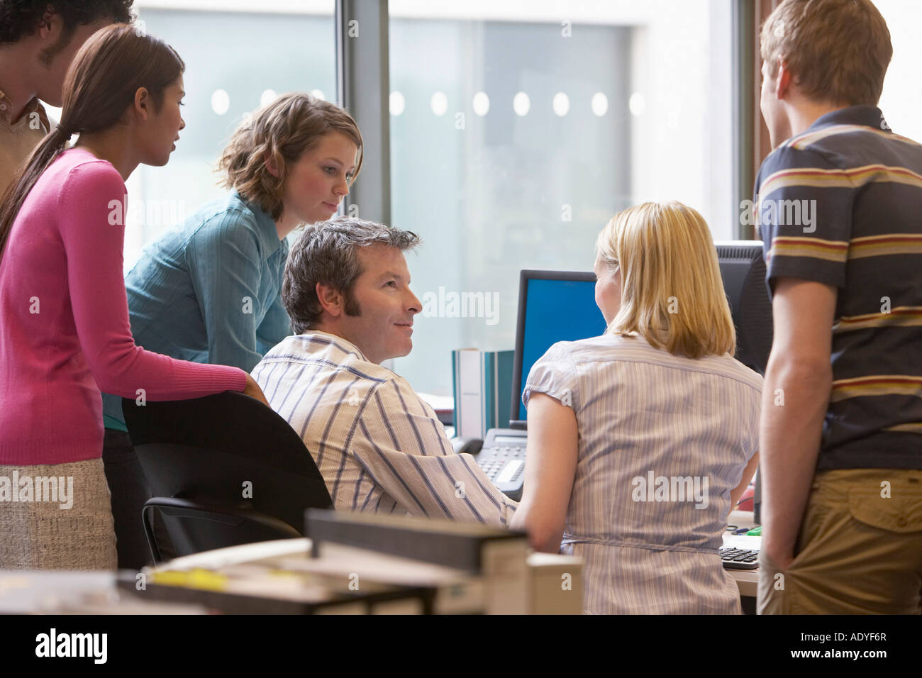 Office workers standing around colleague using computer, back view ...