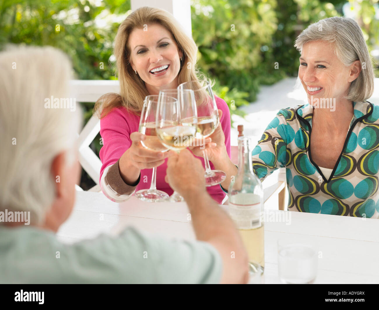 Three people toasting with wine glasses, sitting at verandah table ...