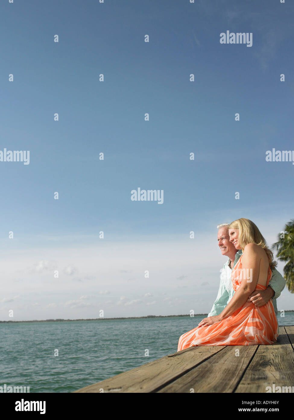 Couple sitting on edge of pier, side view Stock Photo - Alamy
