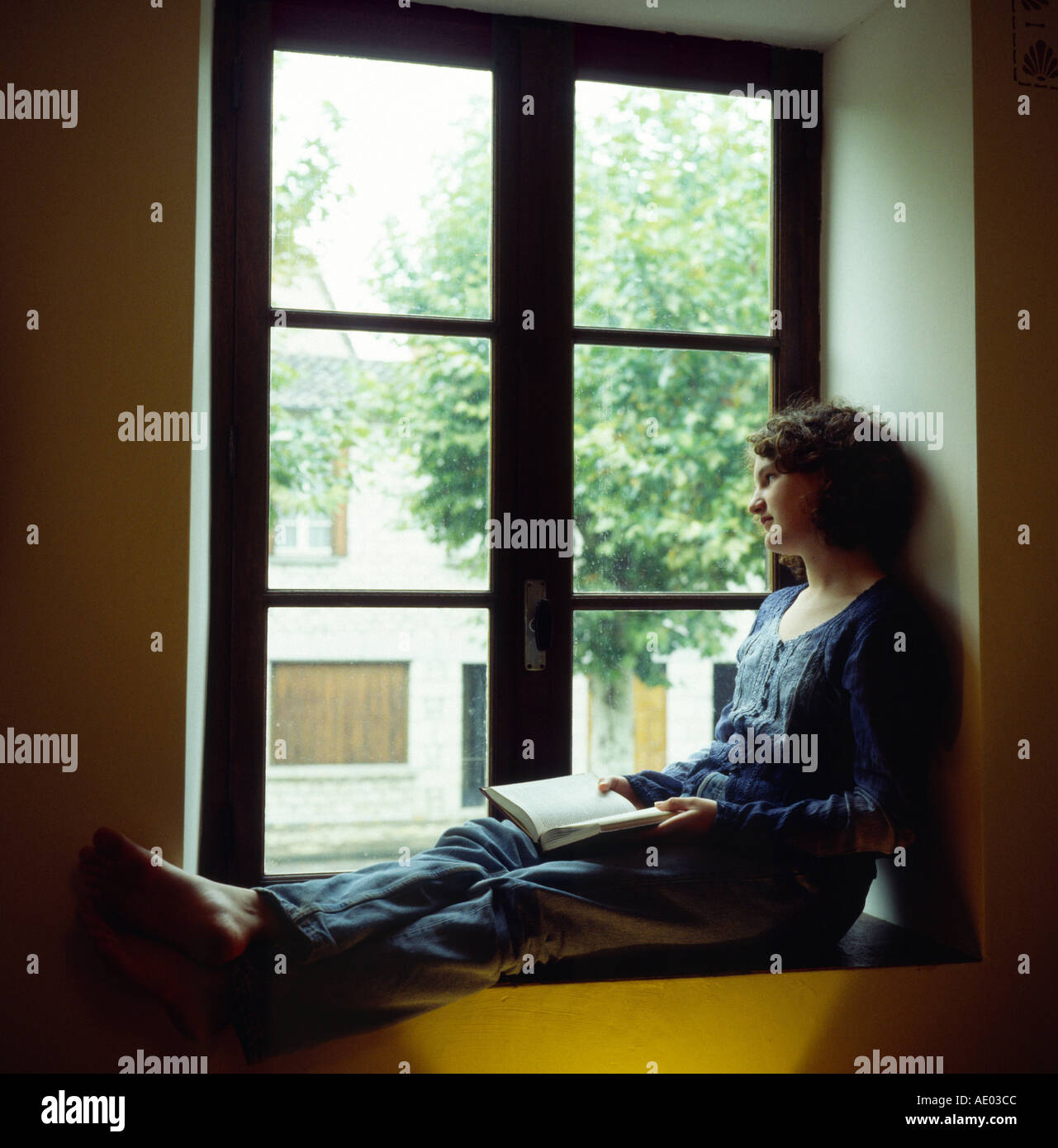 Girl sitting at a window thoughtful Stock Photo - Alamy