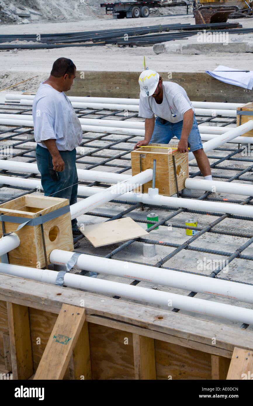 Two laborers placing formwork around rebar and PVC tied together on ...