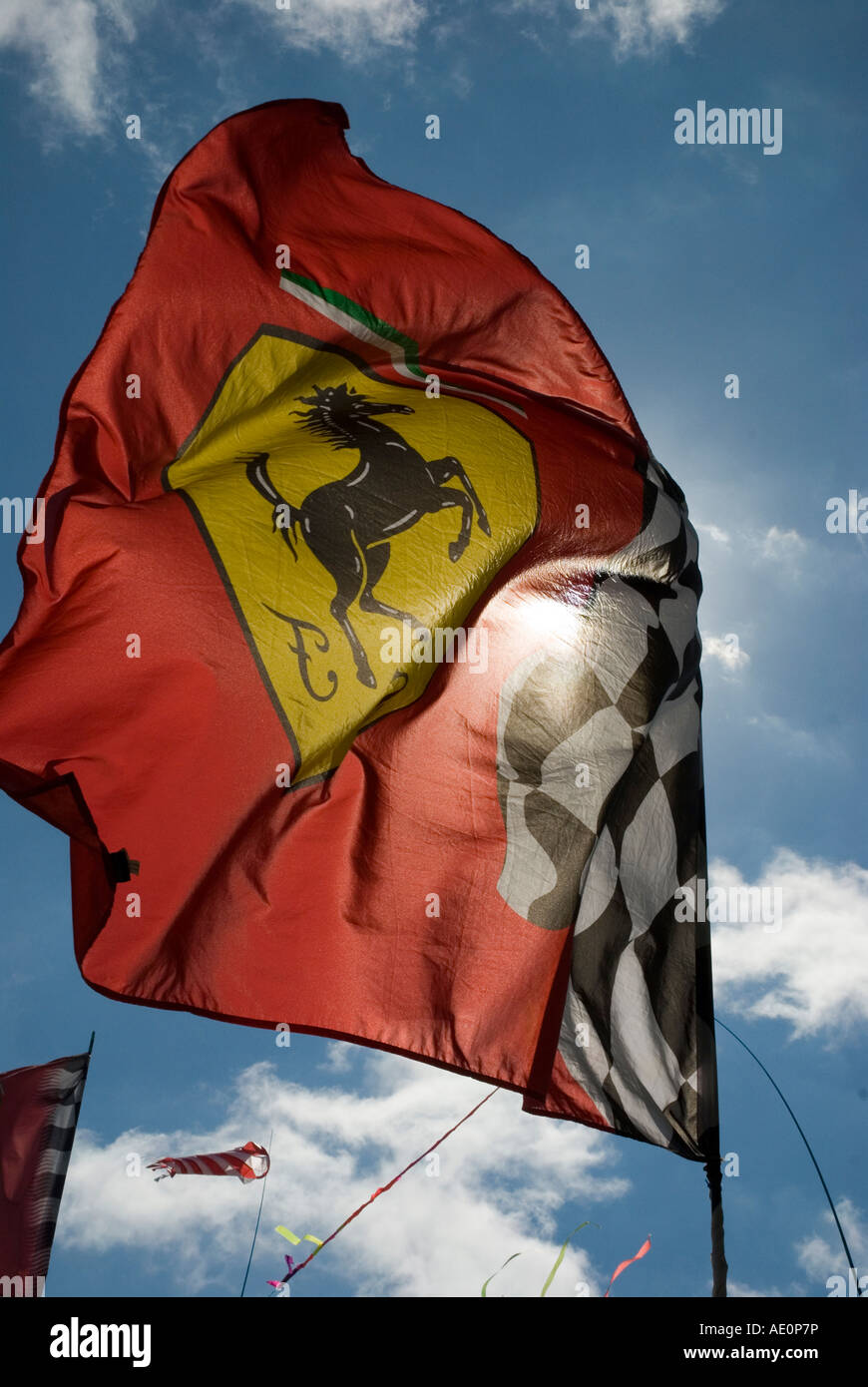 Sun shining through a Ferrari flag against a blue sky with white clouds ...