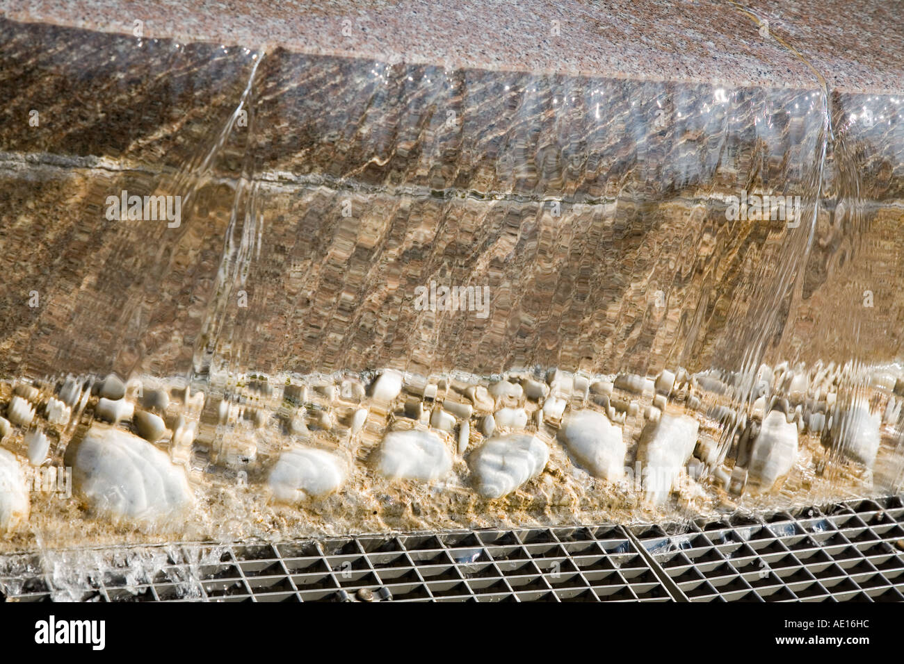 sheet of water tumbling of edge of water feature on to white stones ...