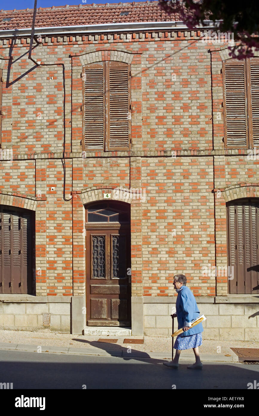 Elderly woman walking with a cane, carrying a fresh baked Baguette ...