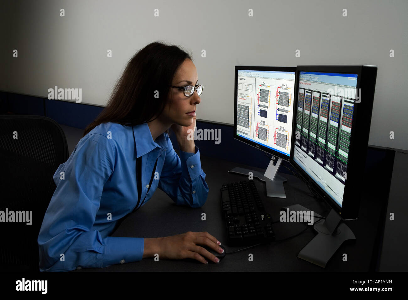A woman sitting at a desk working on a two monitor computer system ...