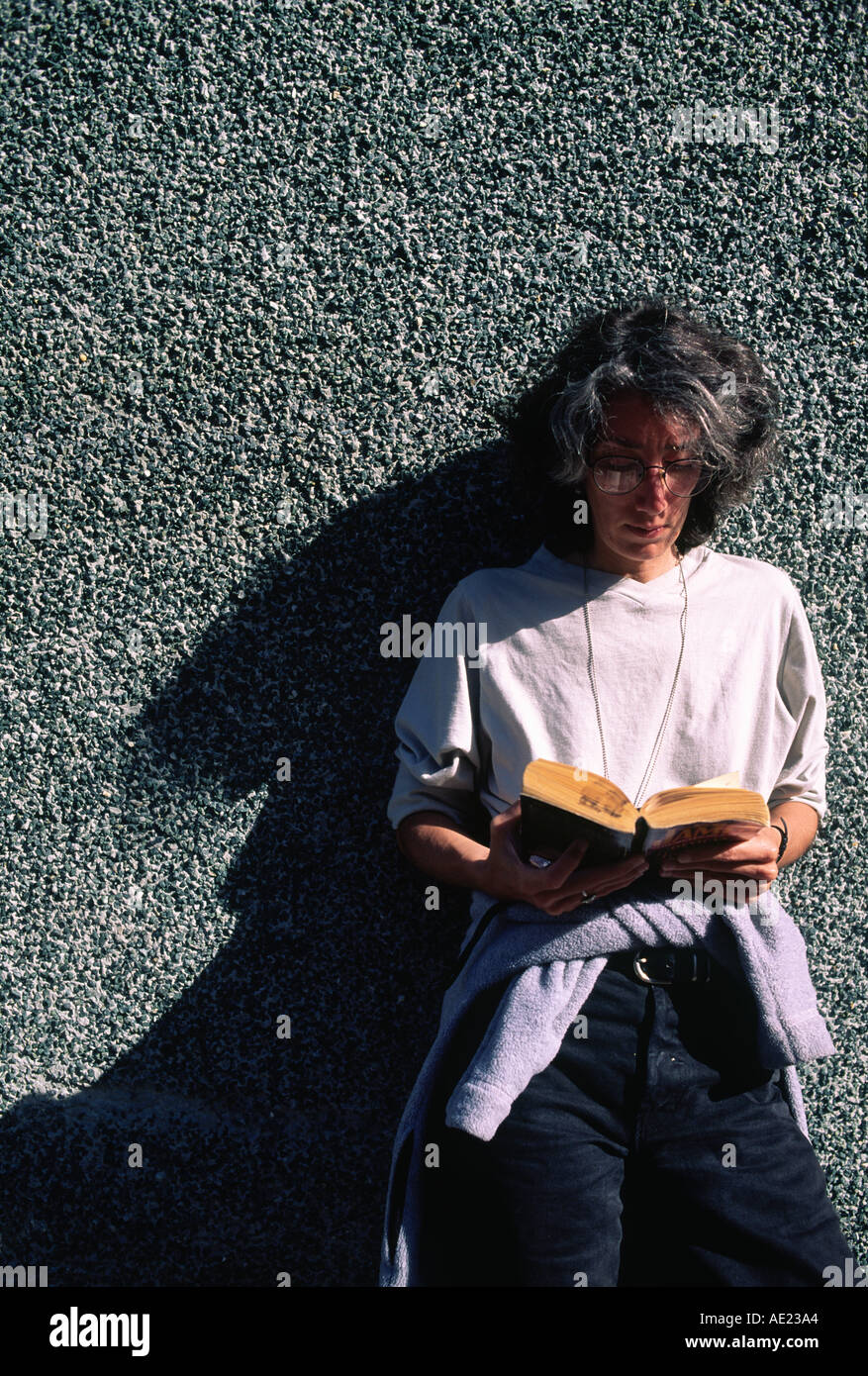 Woman reading a book leaning against a wall Stock Photo - Alamy
