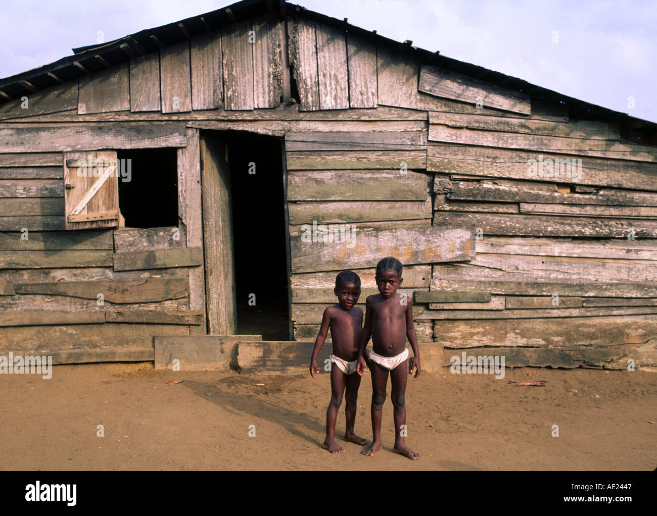 Two children stand in a dusty courtyard in a poor coastal fishing ...