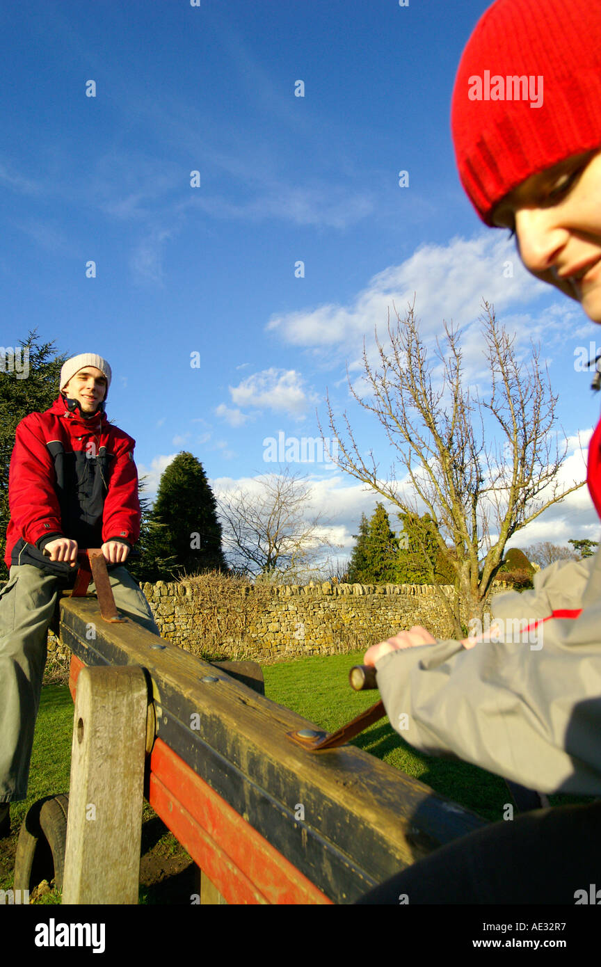 Man and woman in 20s swinging on a seesaw, children playground outdoors ...