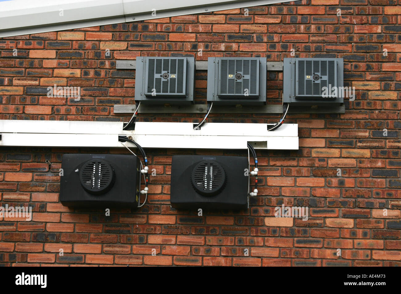 Piped air conditioning units and fans fitted to a building brick wall ...