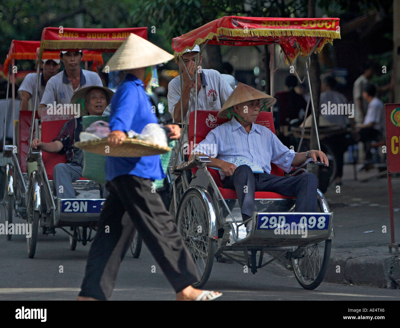 Visitors in cyclo rickshaws tour Hanoi Old Quarter as woman in conical ...