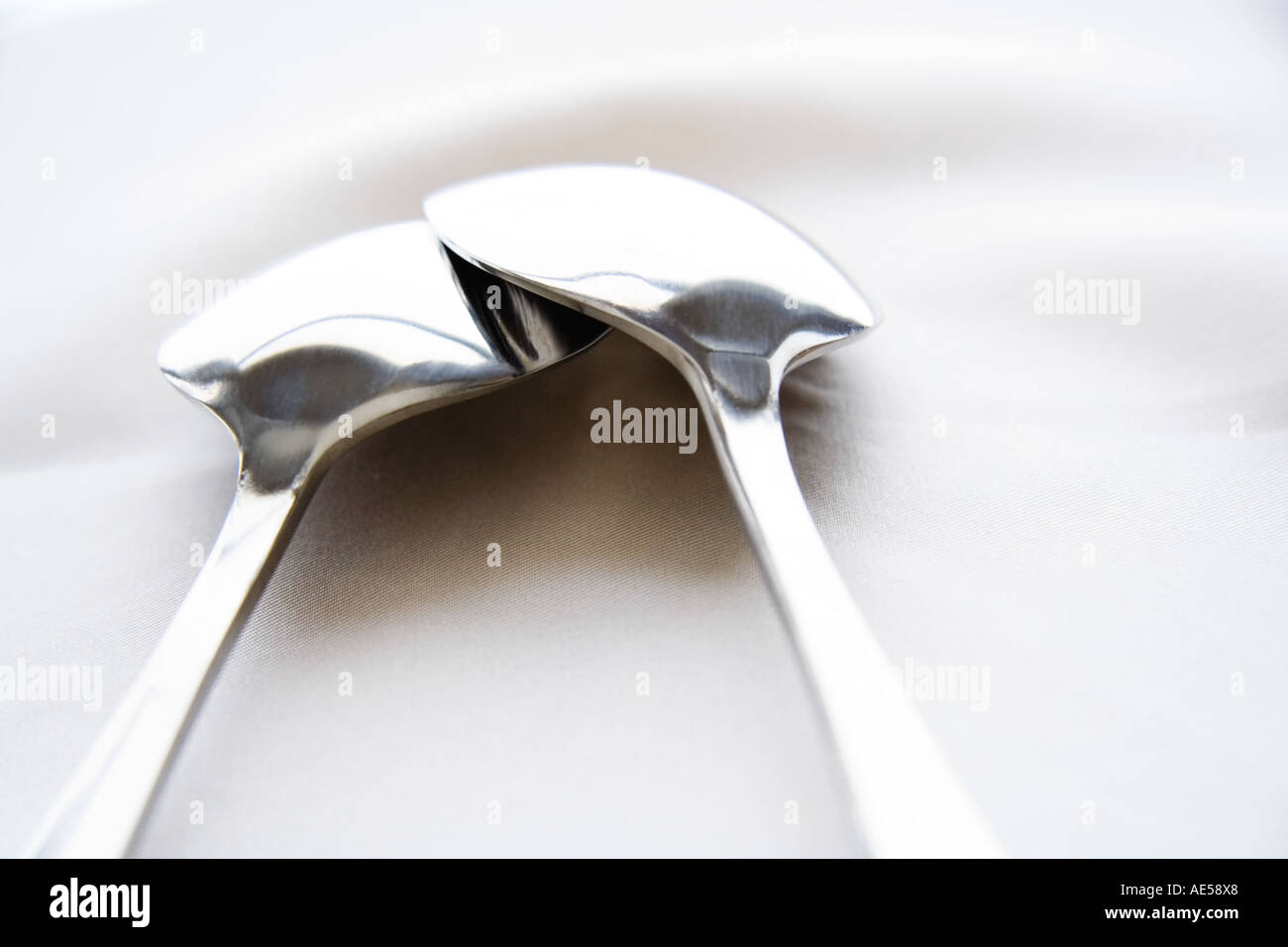 Two silver spoons overlapping on a white silk background Stock Photo ...