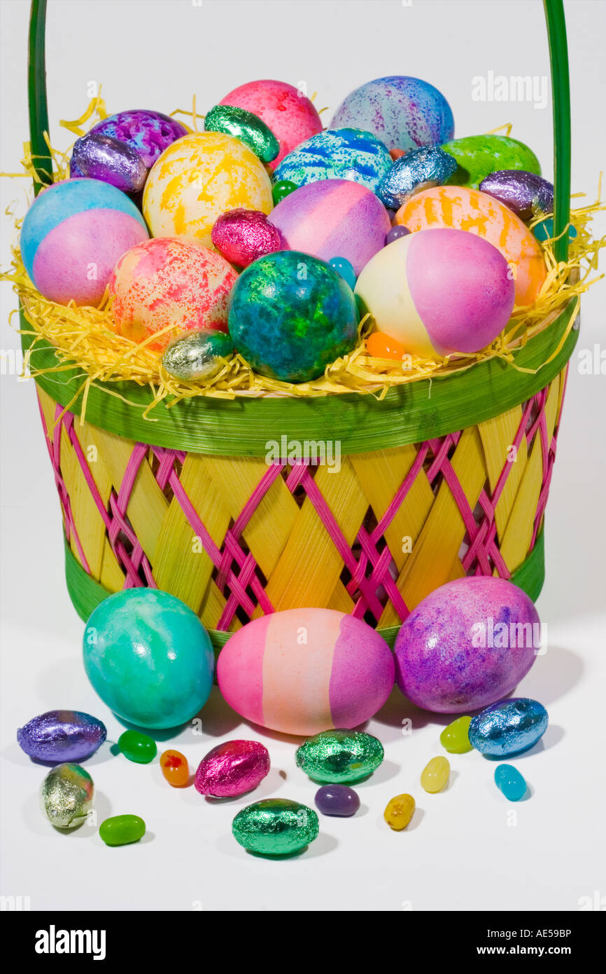 Easter basket filled with coloured eggs and chocolate candies in straw ...