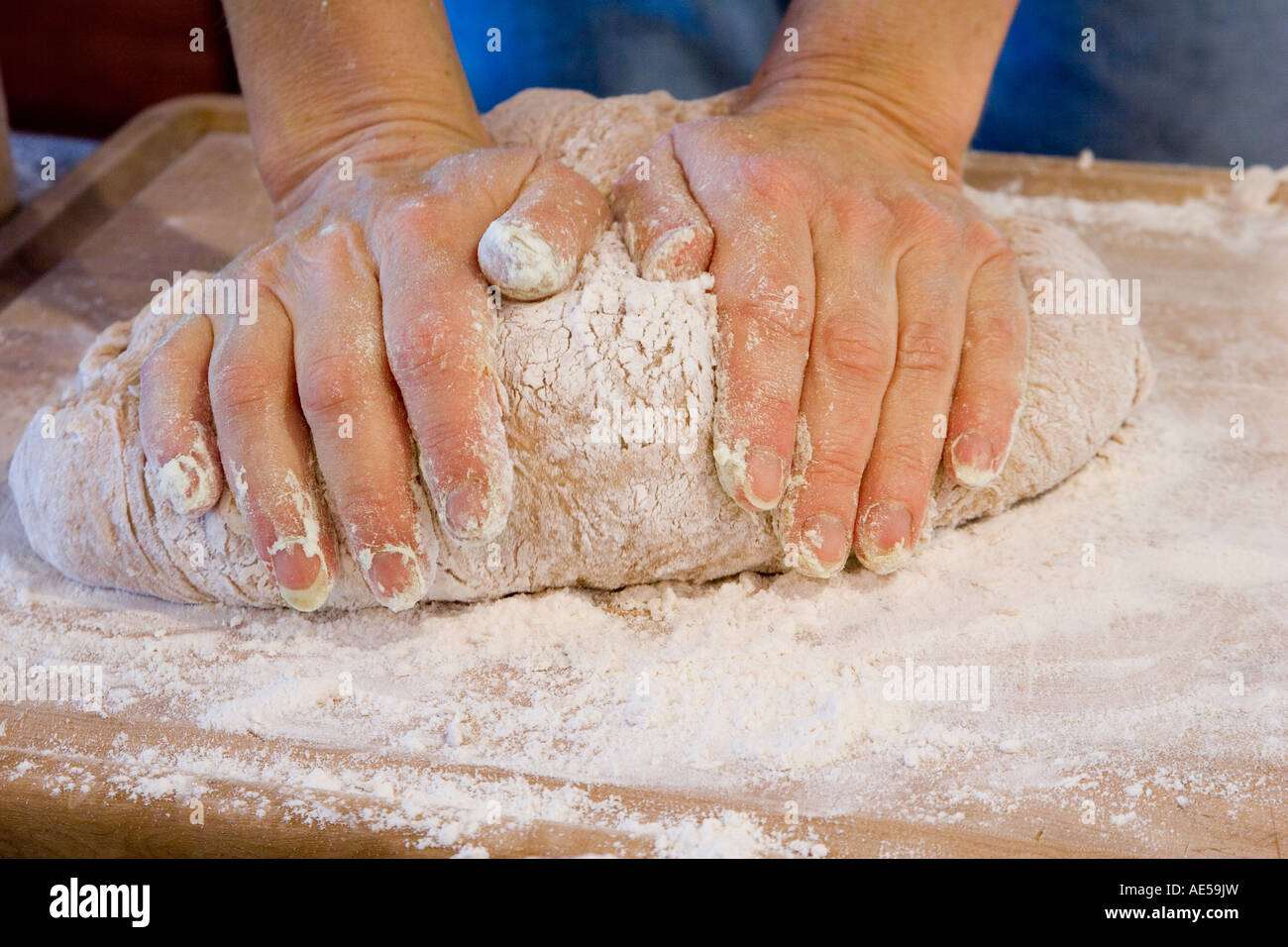 Hands kneading flour into whole wheat bread dough on a wooden cutting ...