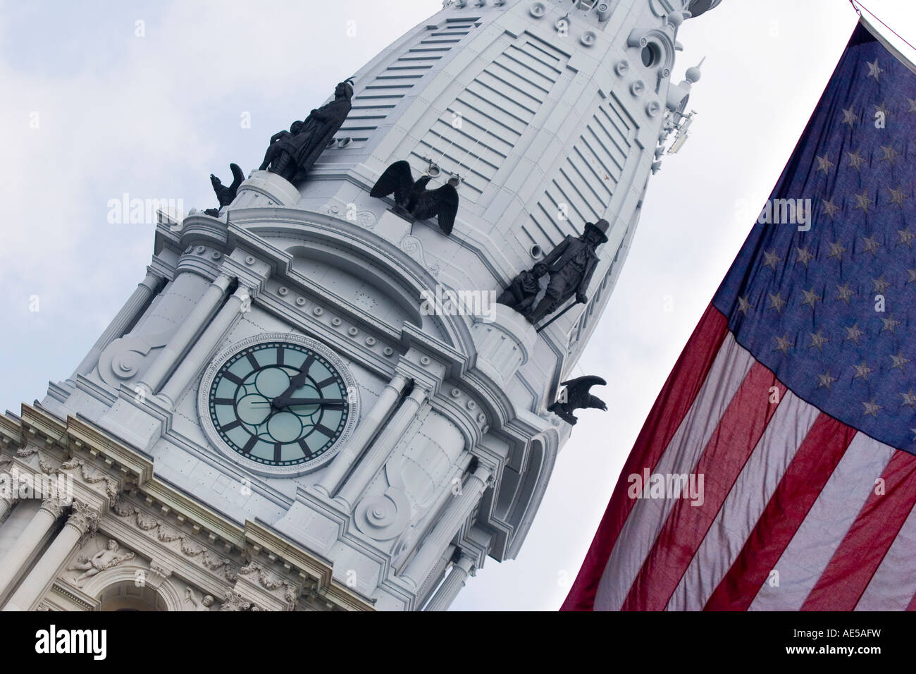 Top of Philadelphia City Hall tower with clock and statues beside flag ...