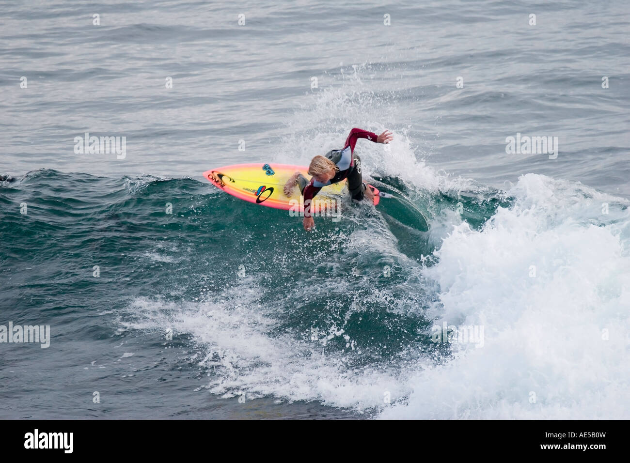 Blond surfer in wet suit twisting on his surfboard as he rides top of a ...