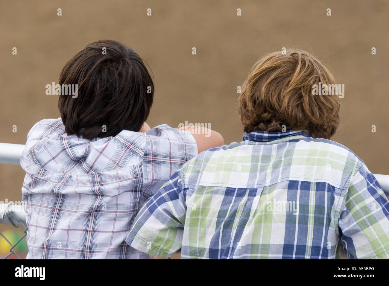 Two boys in plaid shirts leaning on a railing and watching a rodeo ...