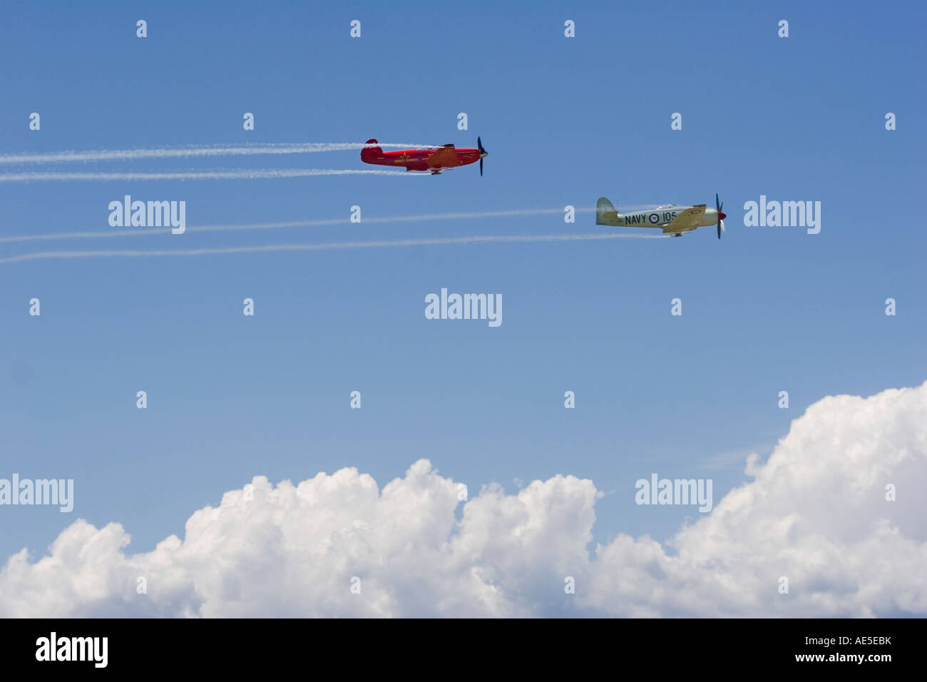 Two small airplanes leaving smoke trails flying across the sky above ...