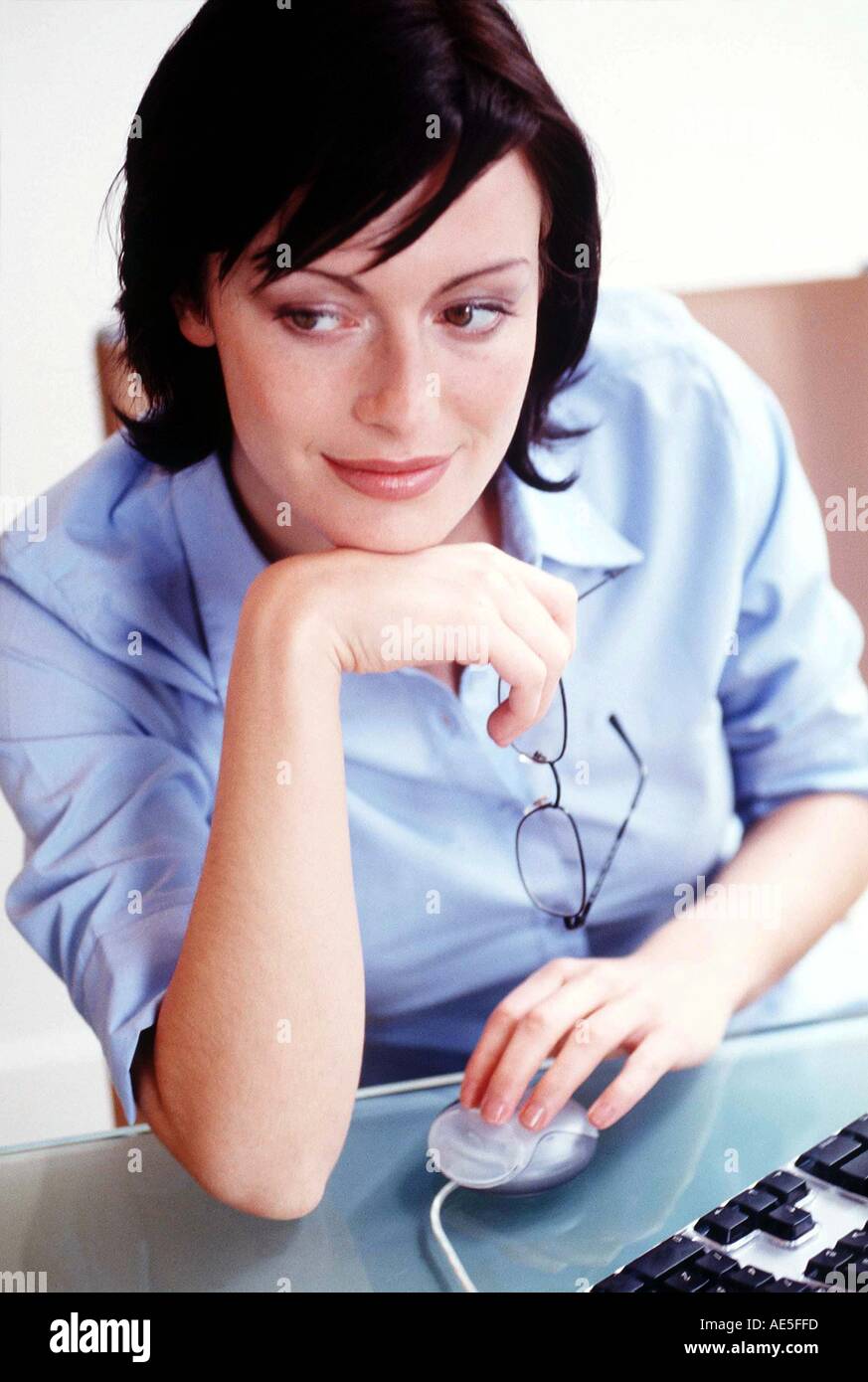 W 18952 01 MODEL RELEASED Female using computer mouse holding glasses ...