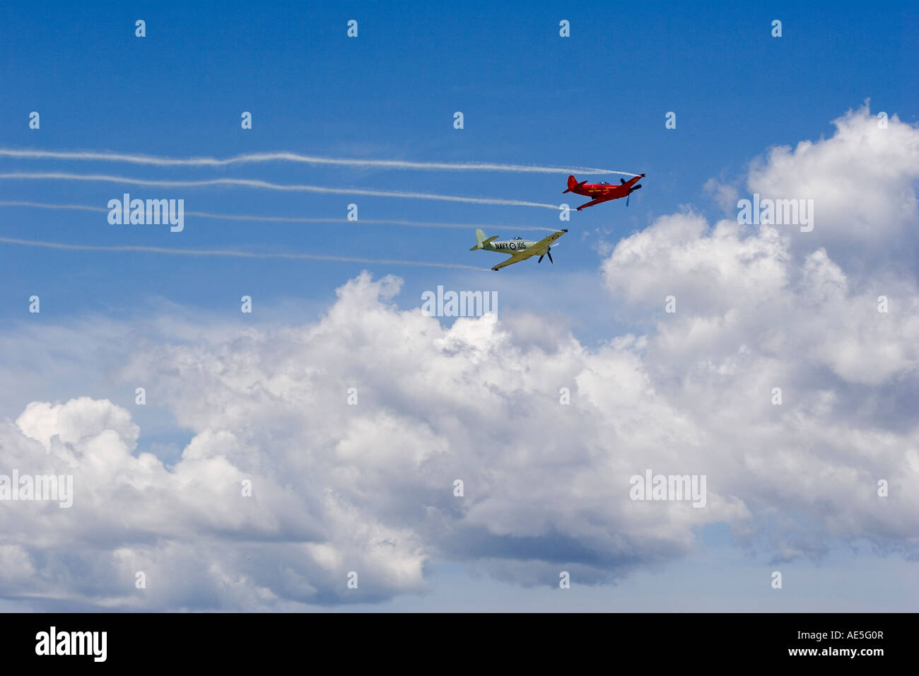Two small airplanes flying across sky into cumulus clouds leaving smoke ...