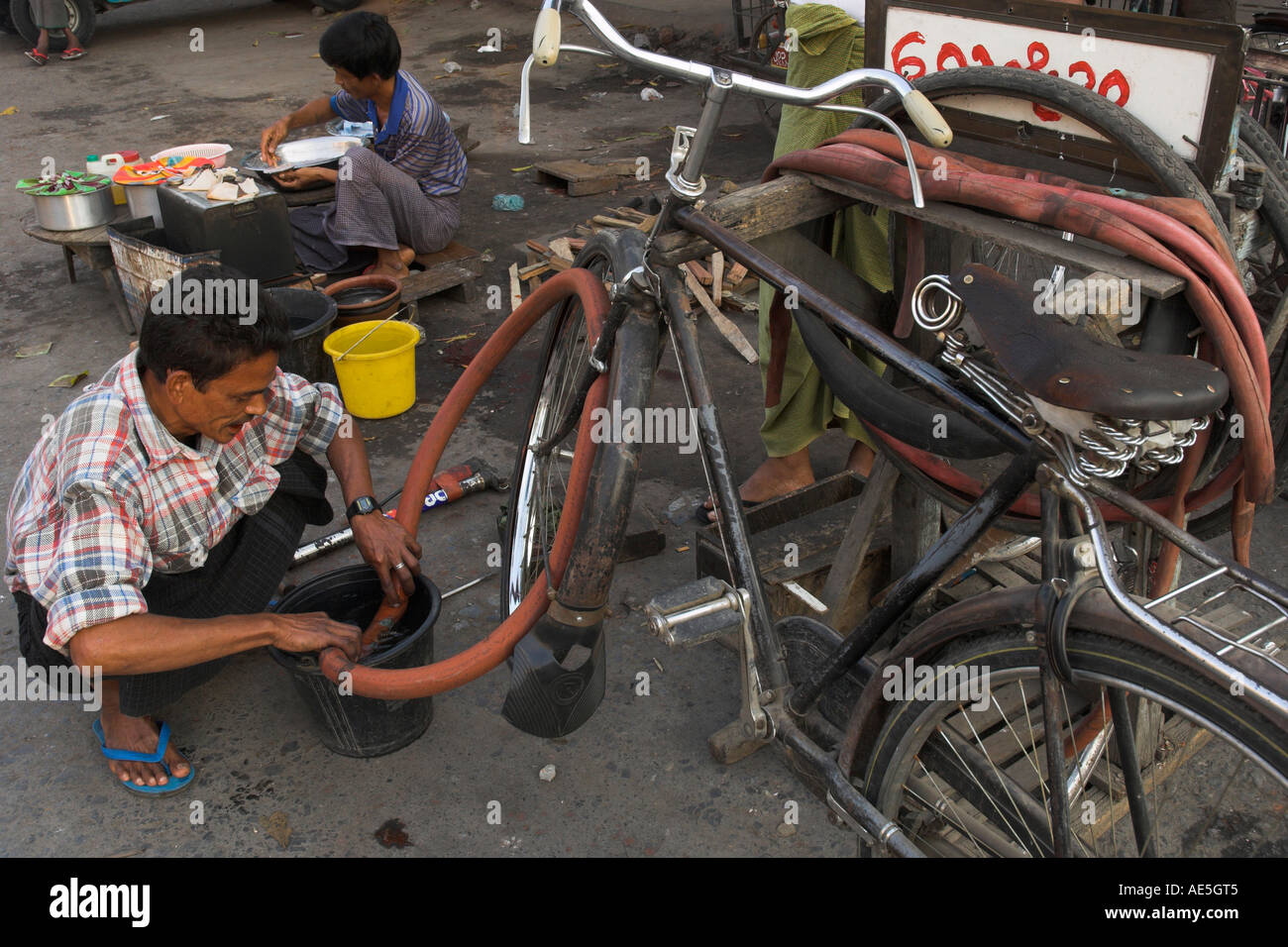Myanmar Burma Mandalay man fixing a puncture on his bike in the street ...