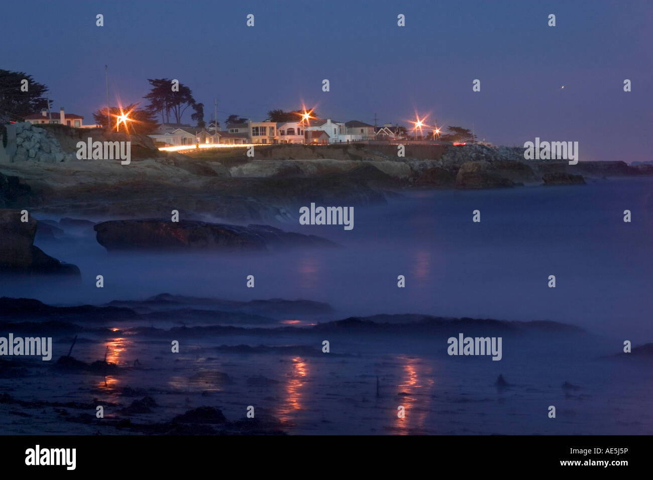 Misty cove along Pacific Ocean coastline at night with lights from ...