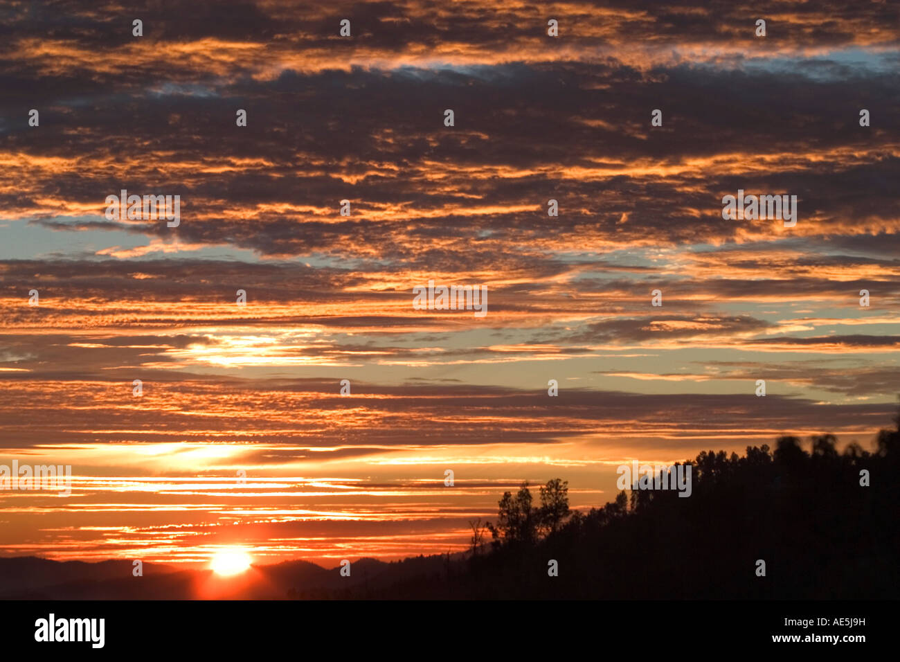 Sun setting over hills lighting up the sky with glowing orange clouds ...