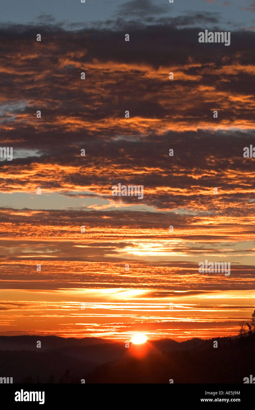 Sun setting over hills lighting up the sky with glowing orange clouds ...