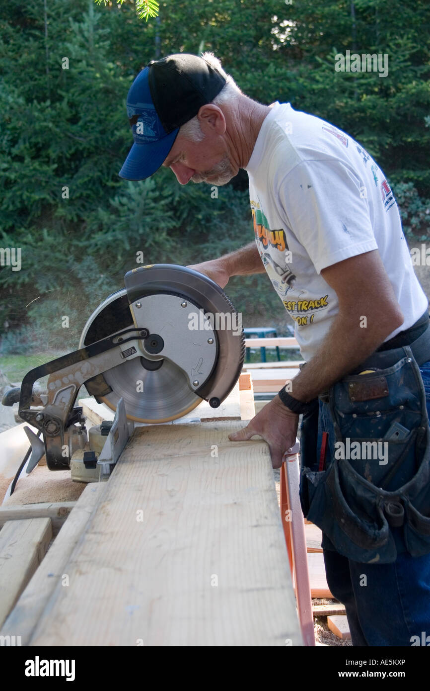 Carpenter in his mid 50s lowering the arm of compound miter saw to cut ...
