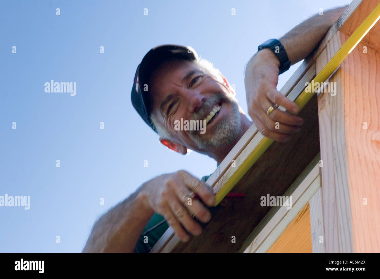 Carpenter in his mid 50s (age 54) leaning over a second story wall with ...
