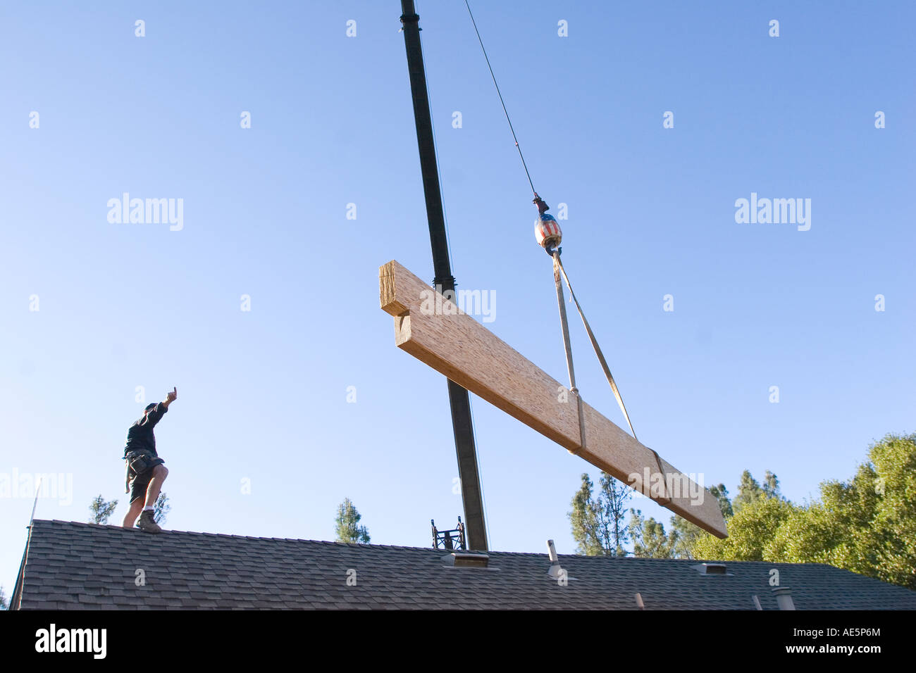 Construction worker standing on roof using hand signals to direct crane ...