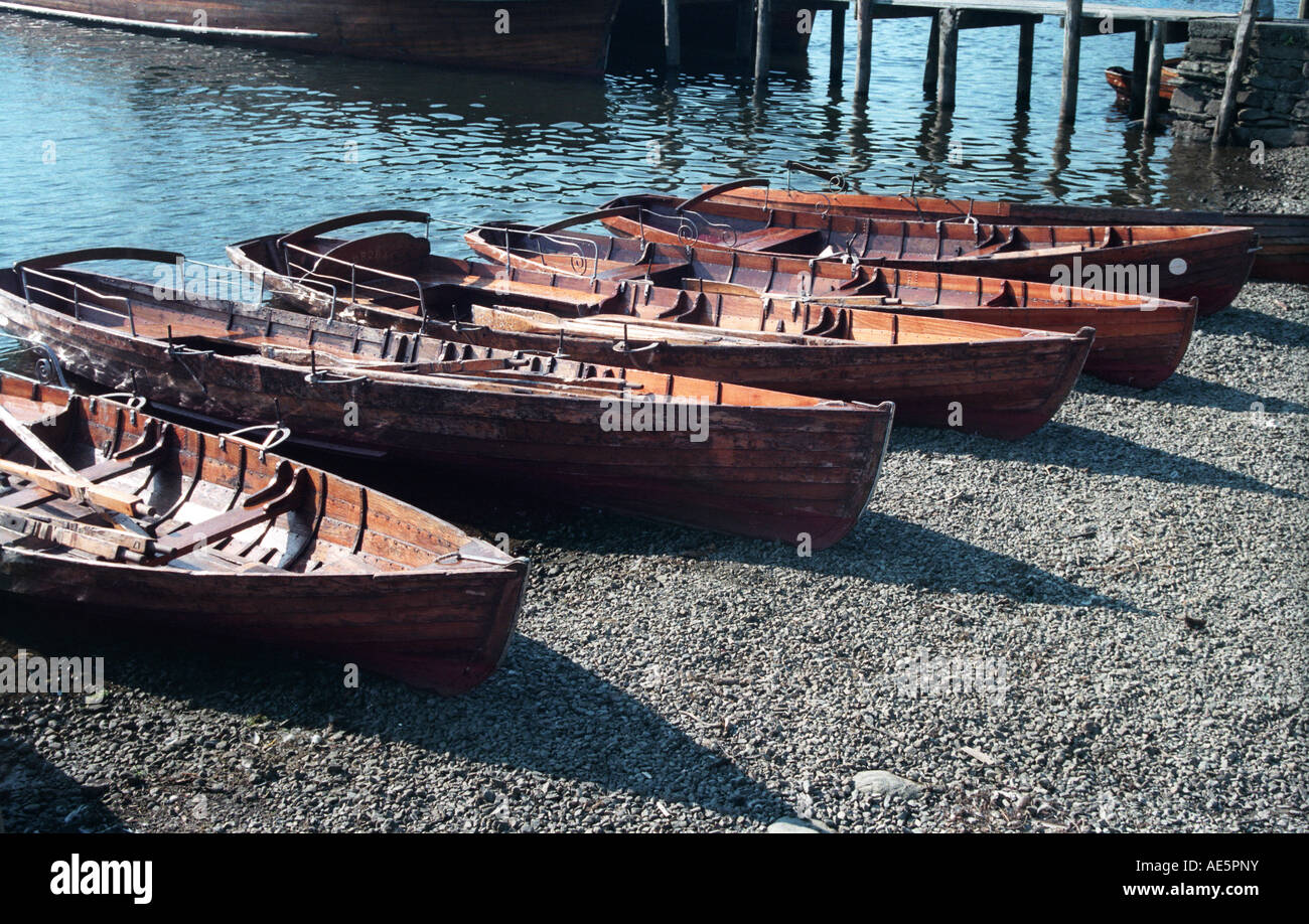 Wooden row boats lined up and casting shadows on the pebble beach along ...