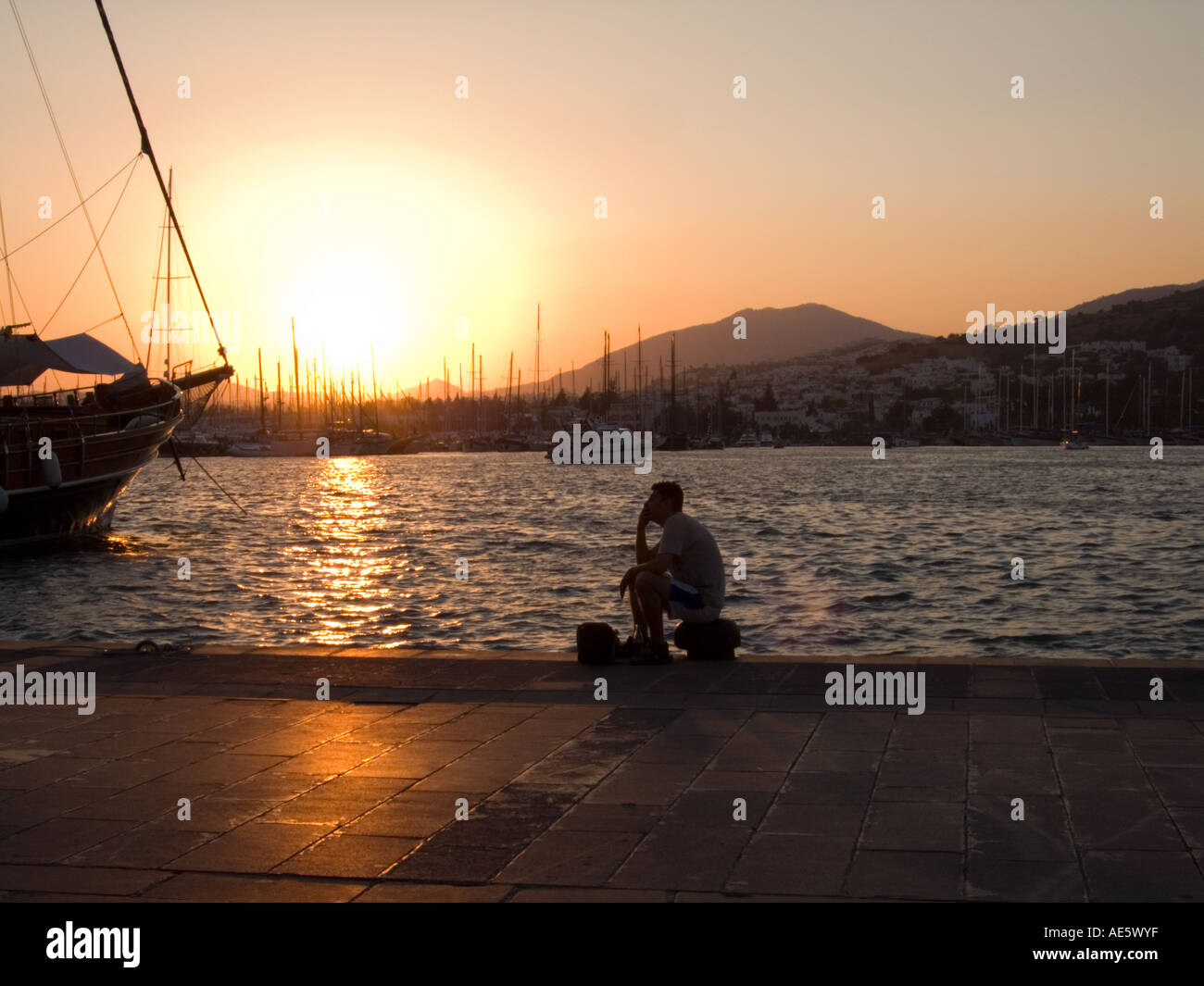Bodrum Harbour at sunset with seated figure by quayside in silhouette ...