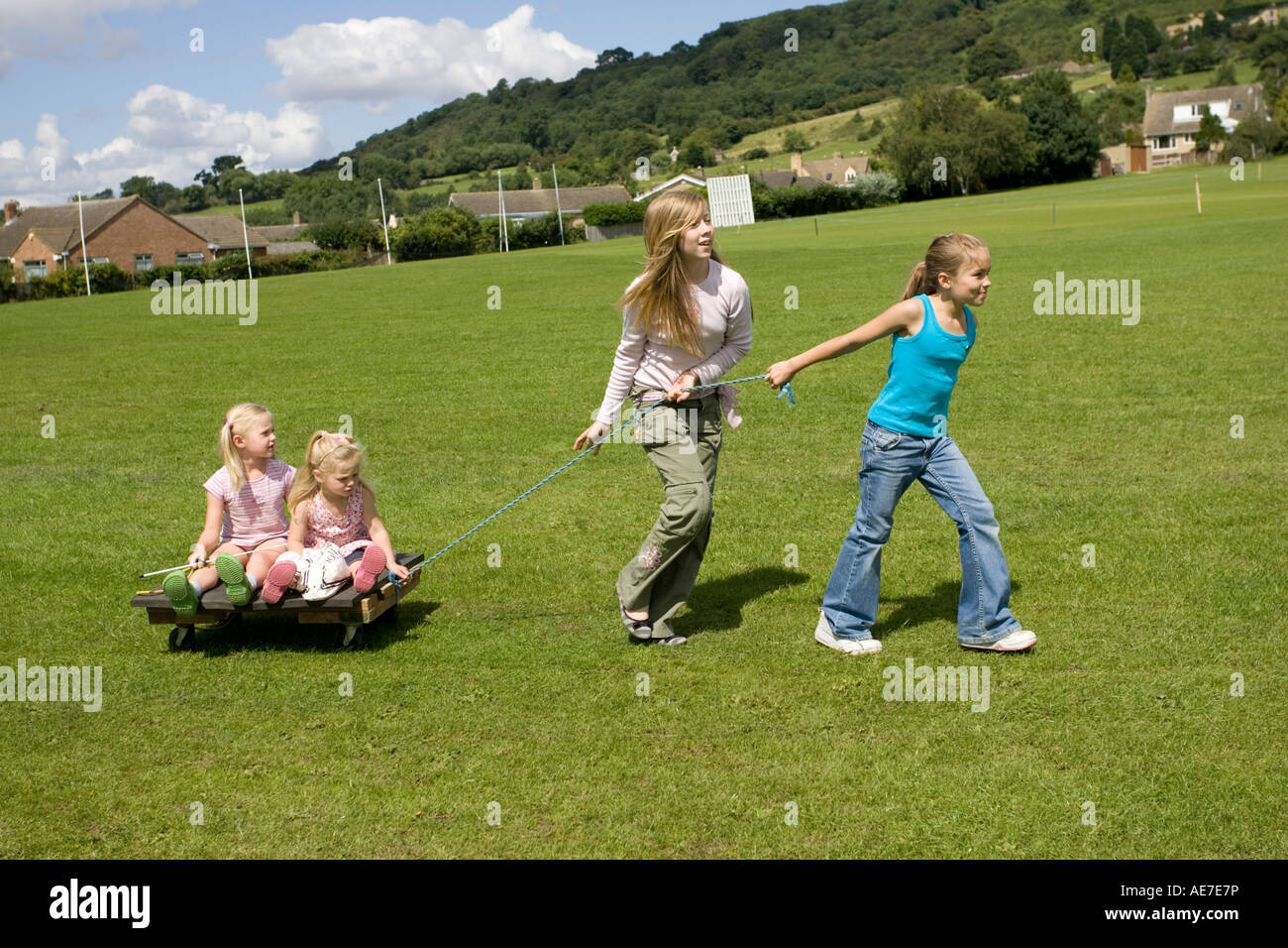 Girls having fun pulling younger sisters across local park on homemade ...