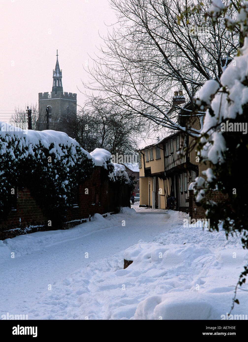 Snow covered village lane with medieval timber frame houses and St Mary ...