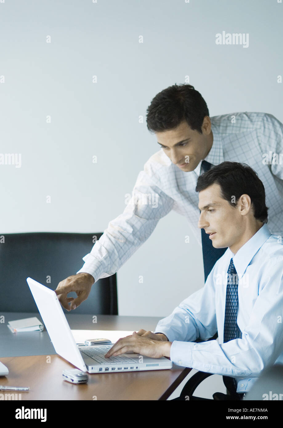 Businessman leaning over colleague's shoulder pointing at laptop screen ...