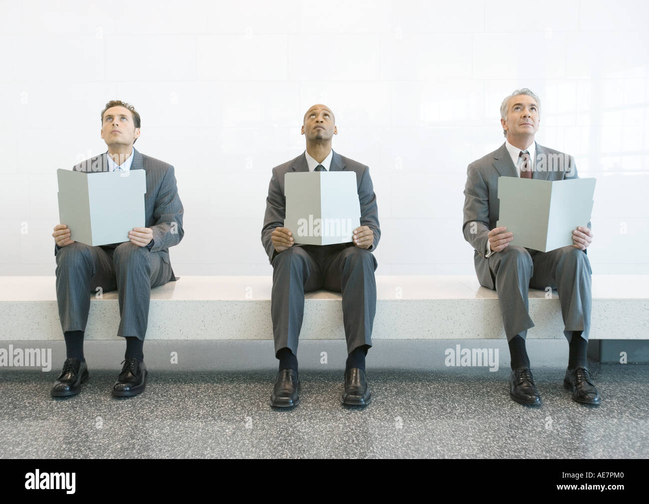 Three men in suits sitting on bench, holding up open folders, and ...
