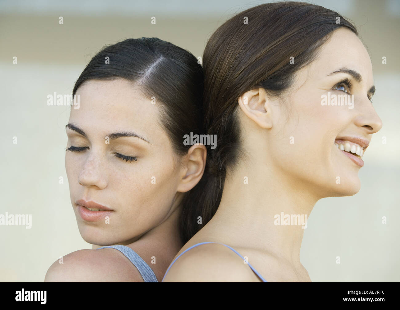 Two young women back to back, one with closed eyes while the other one ...