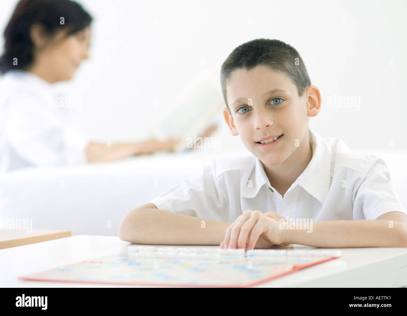 Boy sitting at board game, woman in background Stock Photo - Alamy
