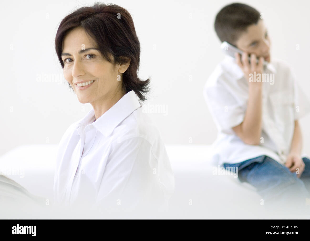 Mature woman smiling, boy in background using cell phone Stock Photo ...