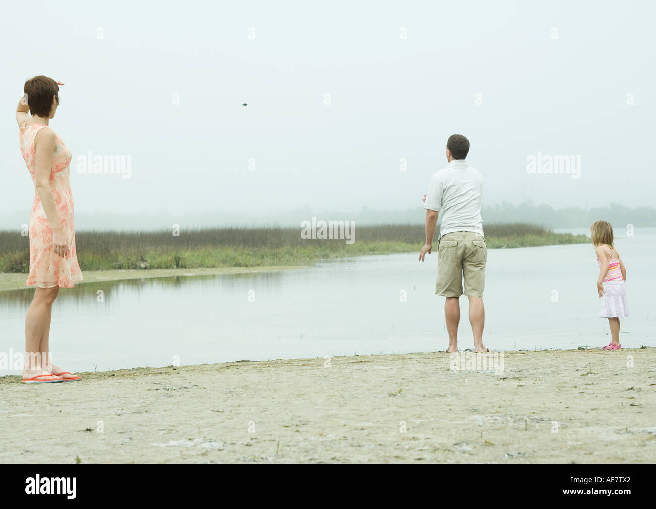 Man throwing pebble into water while family watches Stock Photo - Alamy