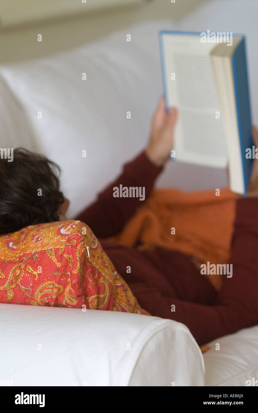 Shot of a woman reclining on a couch while reading a book Stock Photo ...