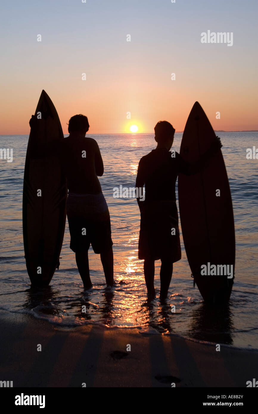 surfers posing with surf board at sunset in a tropical scenic setting ...
