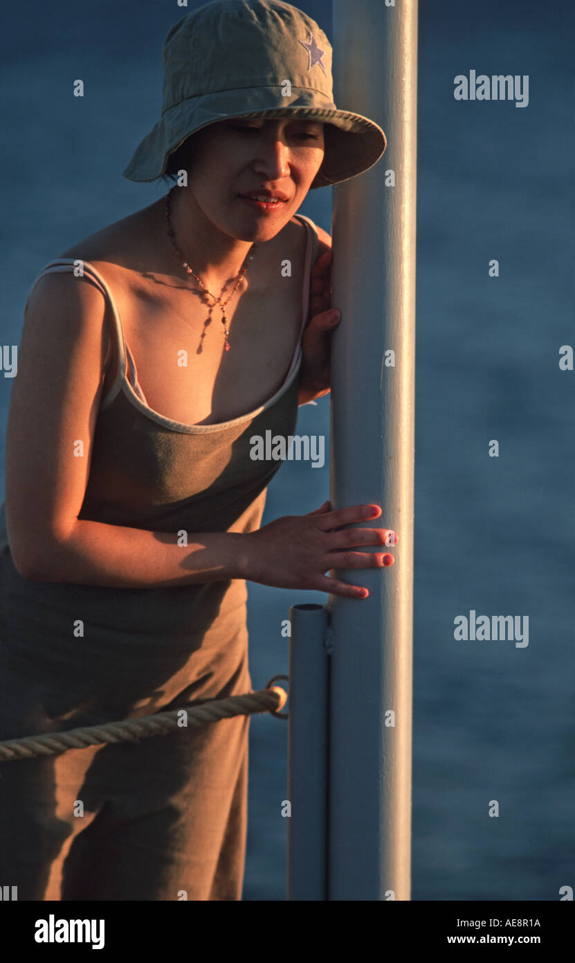 Woman standing on a jetty peering at the fish at sunset Red Sea coast ...