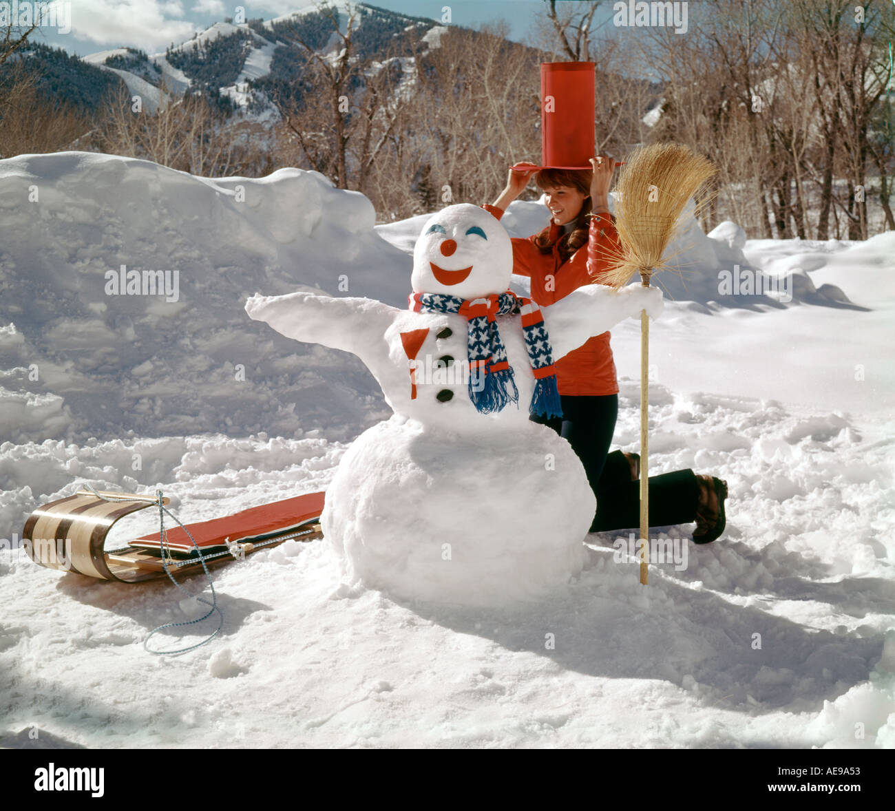 Snowman holding a broom is being decorated by a young woman in a snowy ...
