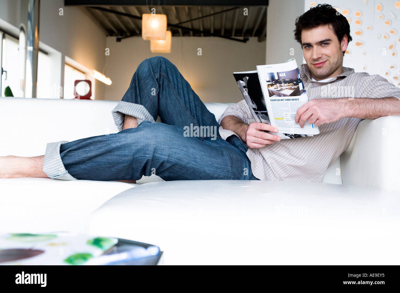 Man lying on a sofa, reading magazine Stock Photo - Alamy