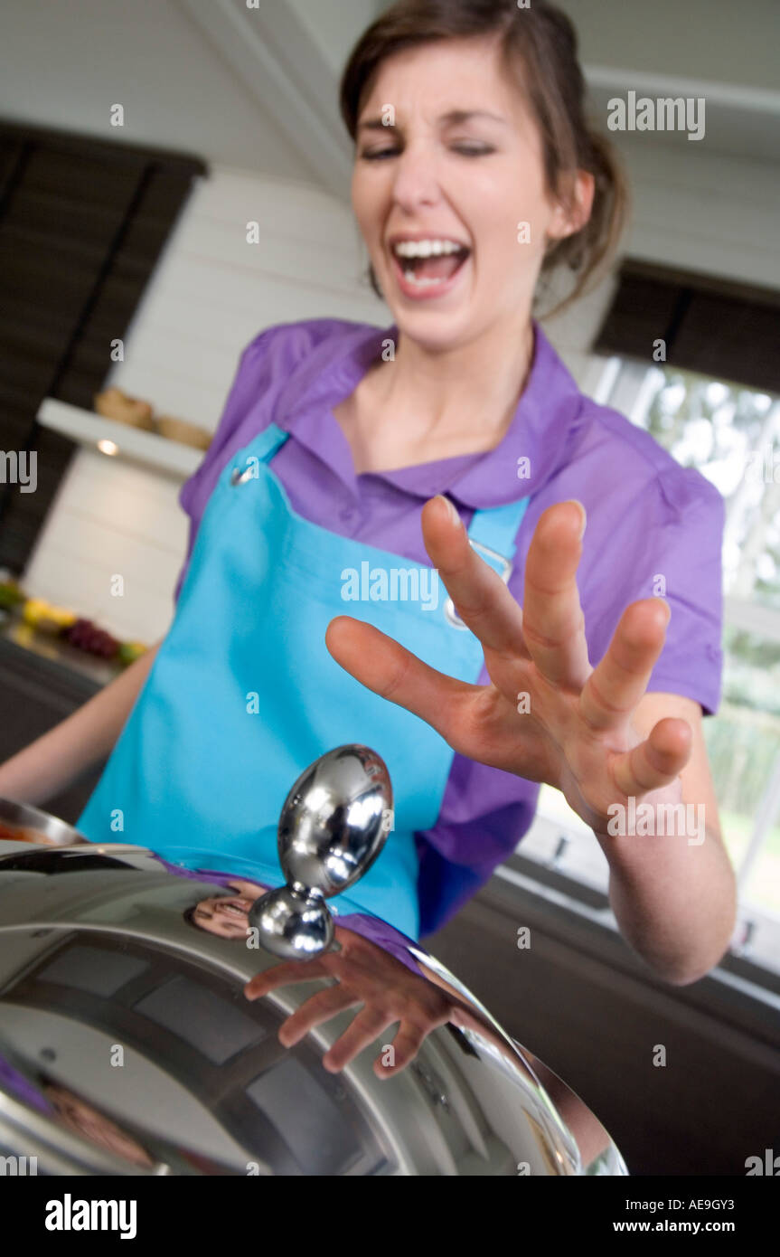 Woman in the kitchen, burning her fingers, trying to lift a pan lid ...