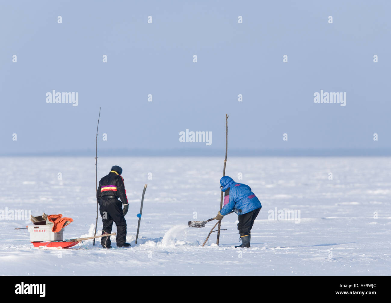 Two fishermen clearing the snow from the hole in the ice for fishing ...